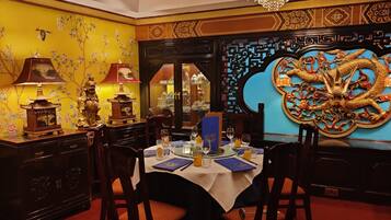 Uma sala de jantar com uma mesa posta para quatro pessoas, rodeada por decoração tradicional e um grande mural de dragão.