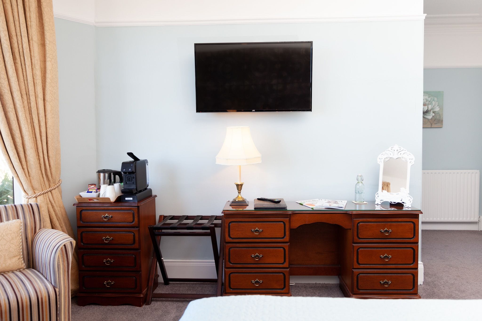 Quarto de hotel com televisão de tela plana na parede, uma escrivaninha com abajur, uma cadeira e uma cama.