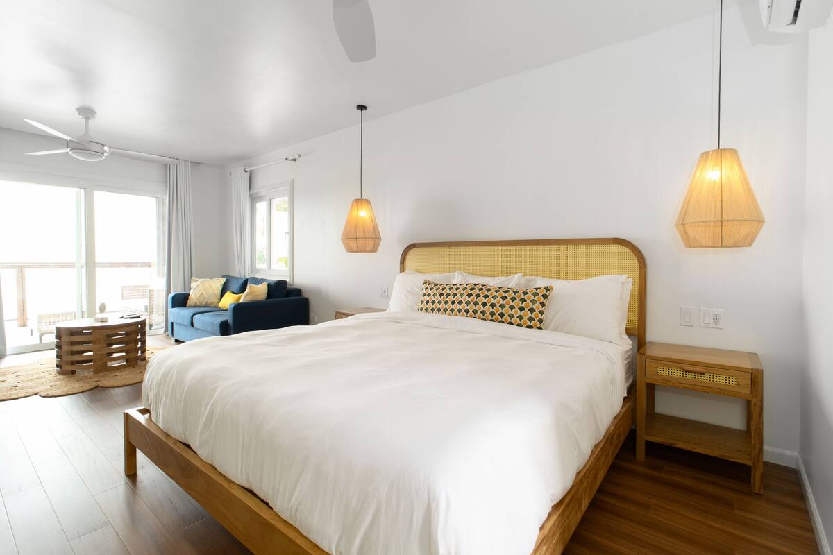Quarto com uma cama grande, uma mesa de cabeceira de madeira, um sofá azul e um ventilador de teto.