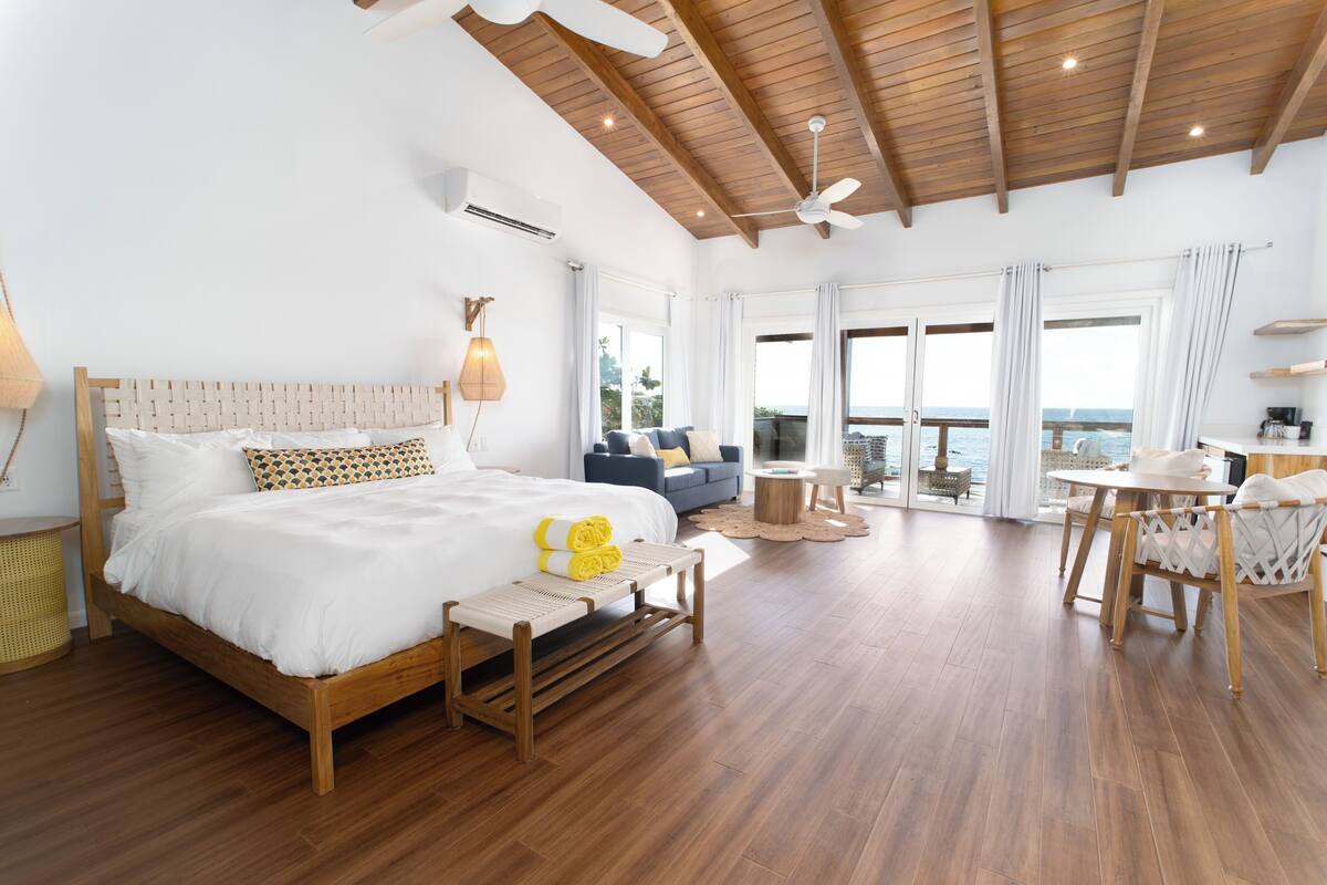 Um quarto espaçoso com cama de madeira, ventilador de teto, janela grande e varanda com vista.
