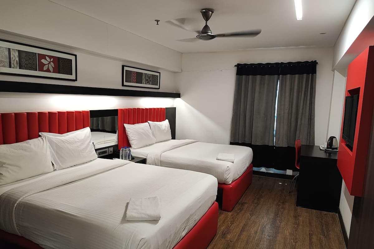 Quarto de hotel com duas camas, uma escrivaninha, uma cadeira, televisão e ventoinha no teto.