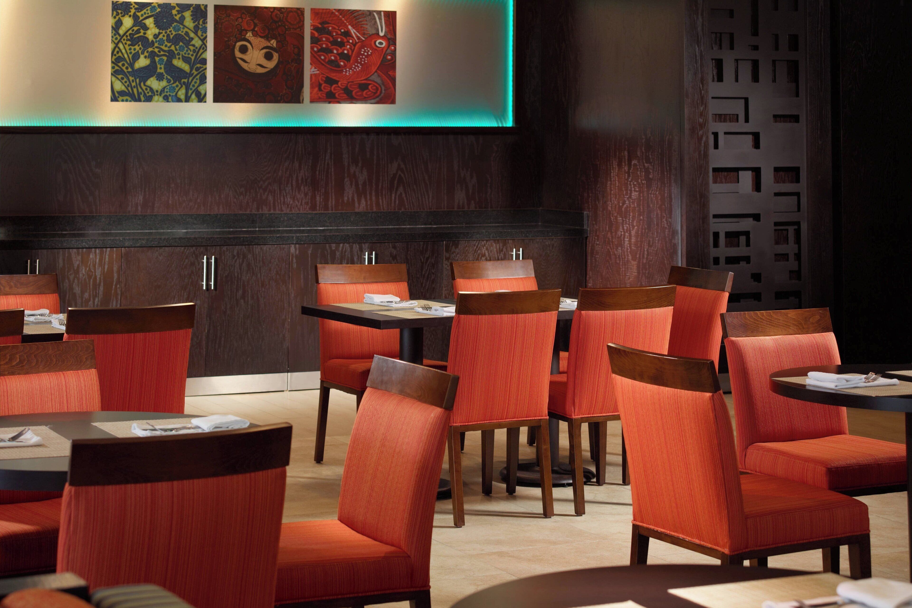 Um restaurante com cadeiras e mesas estofadas em vermelho, armários de madeira e obras de arte decorativas nas paredes.