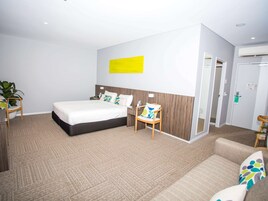 Quarto de hotel com uma cama grande, mesa de cabeceira de madeira, uma cadeira e um sofá.