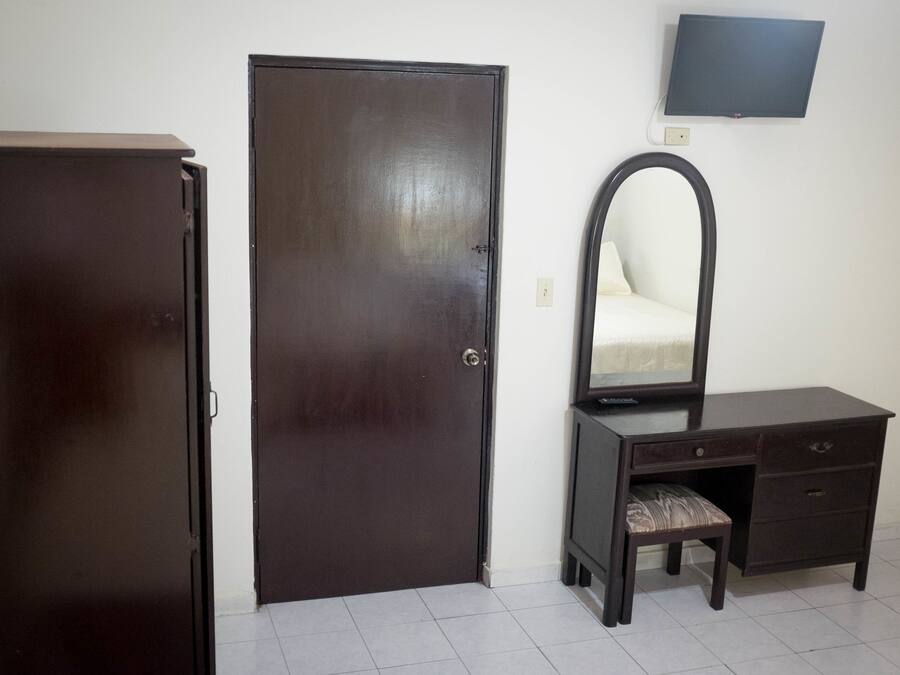 Quarto com guarda-roupa fechado, penteadeira com espelho e televisão de tela plana presa na parede.