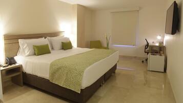 Quarto de hotel com uma cama grande, mesa de cabeceira com telefone, escrivaninha com computador e um pequeno frigorífico.