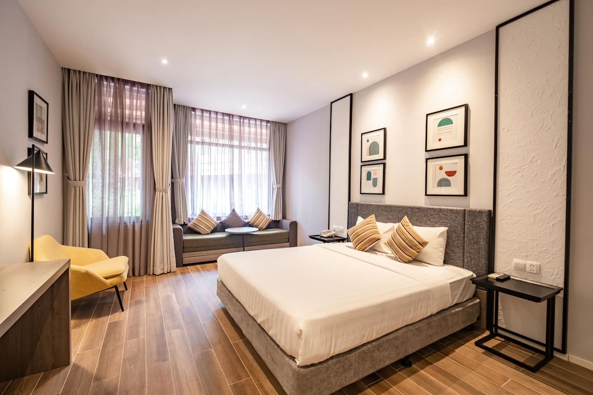 Quarto de hotel moderno com uma cama grande, um sofá, uma escrivaninha e uma janela com cortinas.