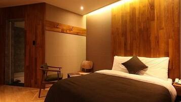 Quarto moderno com cabeceira de madeira, cama com travesseiros brancos e escuros, mesa de cabeceira com abajur e uma cadeira.