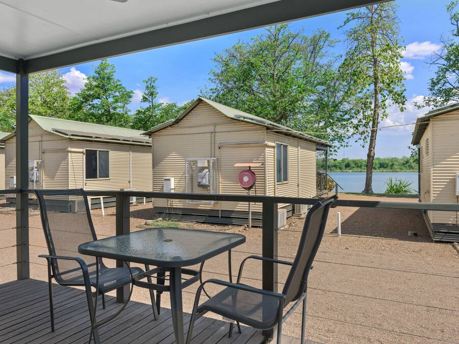 Uma área externa coberta com mesa e cadeiras, com vista para um lago e várias casas móveis.