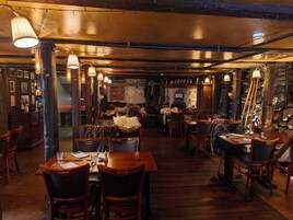 Interior de restaurante com mesas e cadeiras de madeira, luminárias pendentes e parede de pedra.