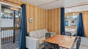 Um quarto com parede revestida de madeira, um sofá, uma mesa de jantar com cadeiras e uma janela com cortinas.
