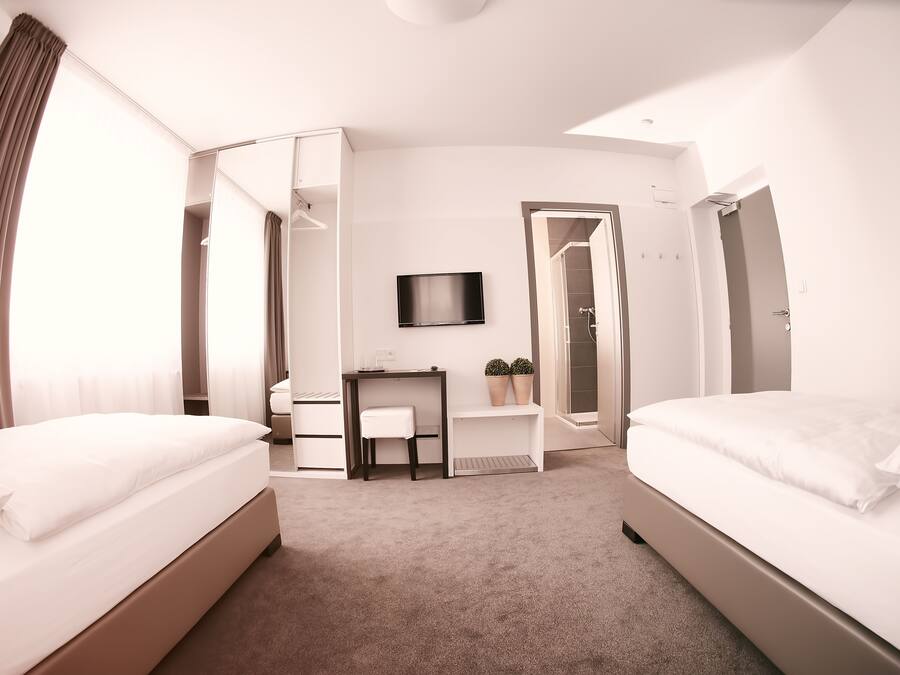 Quarto de hotel com duas camas, uma mesa, televisão e área de chuveiro.
