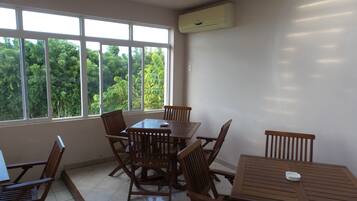 Quarto com uma grande janela, ventoinha no teto e uma mesa com cadeiras.