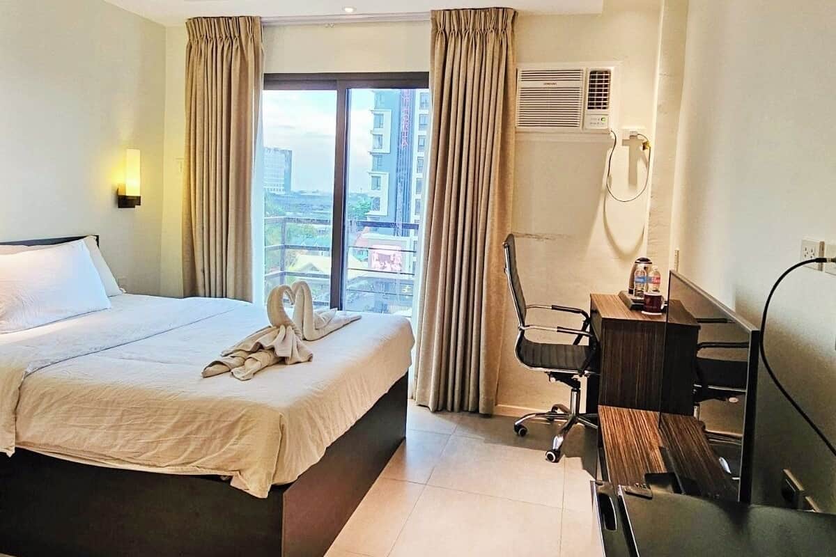 Quarto de hotel com cama, escrivaninha, cadeira, ar condicionado e vista para a cidade.
