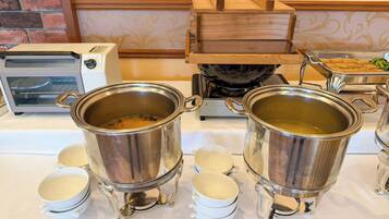Disposição de buffet com duas grandes panelas de metal, várias tigelas brancas e um forno elétrico tostador.