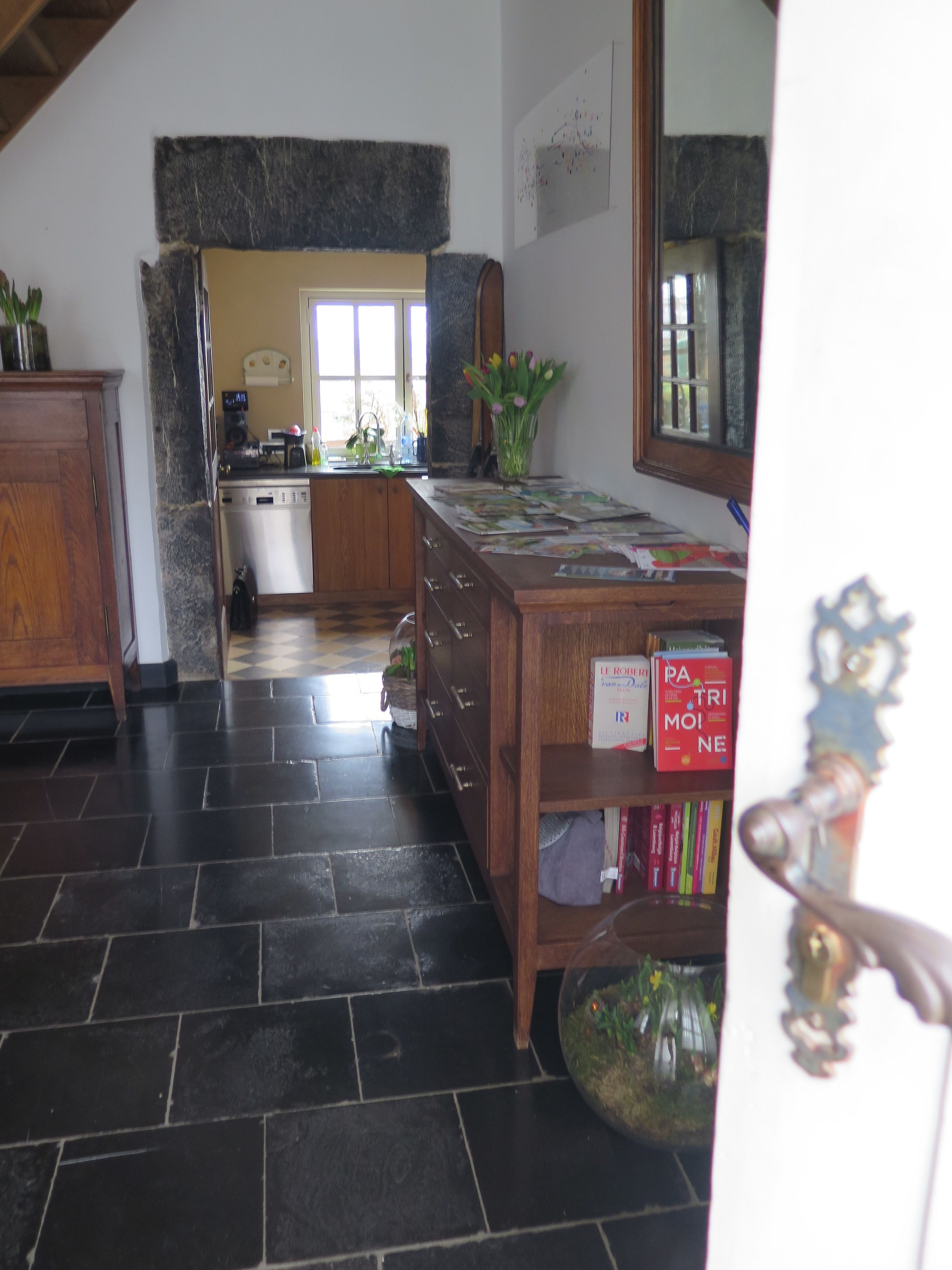 Uma cozinha com soalho de azulejos escuros, um armário de madeira, uma pia e uma janela.