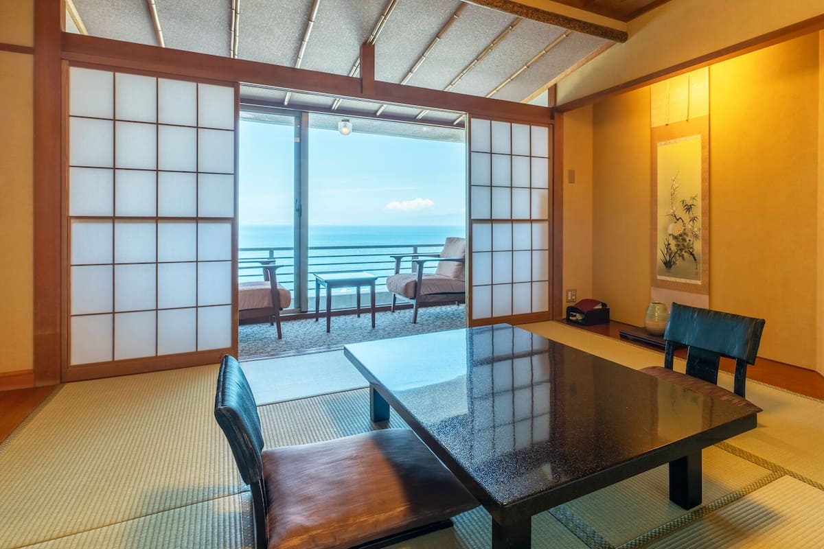 Um quarto com tatames, uma mesa baixa, um banco e vista para o mar.