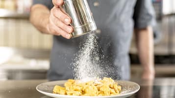 Alguém polvilhando sal sobre um prato de comida.