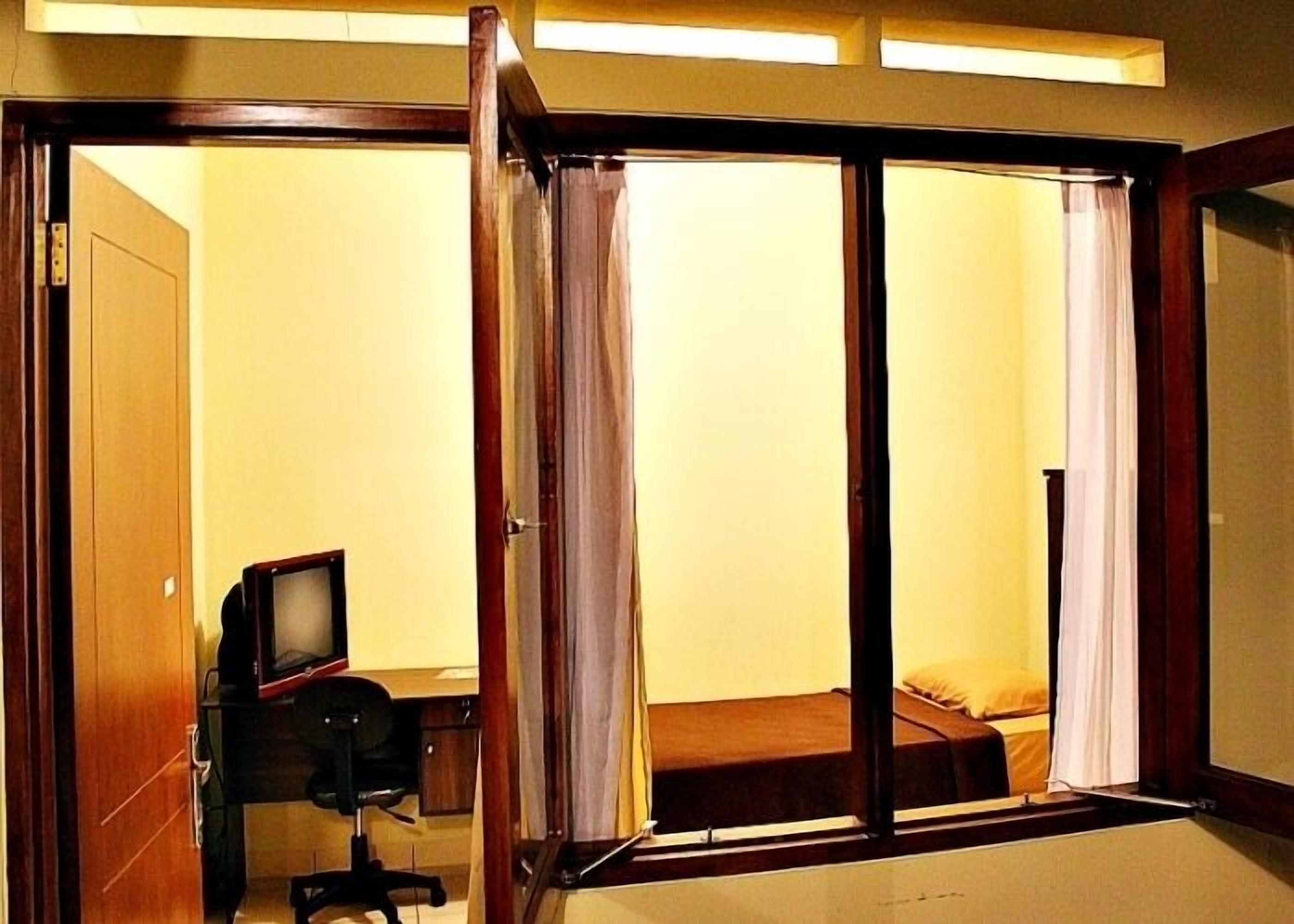 Quarto de hotel com uma cama, uma mesa de escritório com computador e uma televisão.
