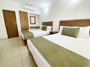 Quarto de hotel com duas camas de solteiro, uma cama de casal, cabeceira de madeira, mesa de cabeceira, espelho e ar condicionado.