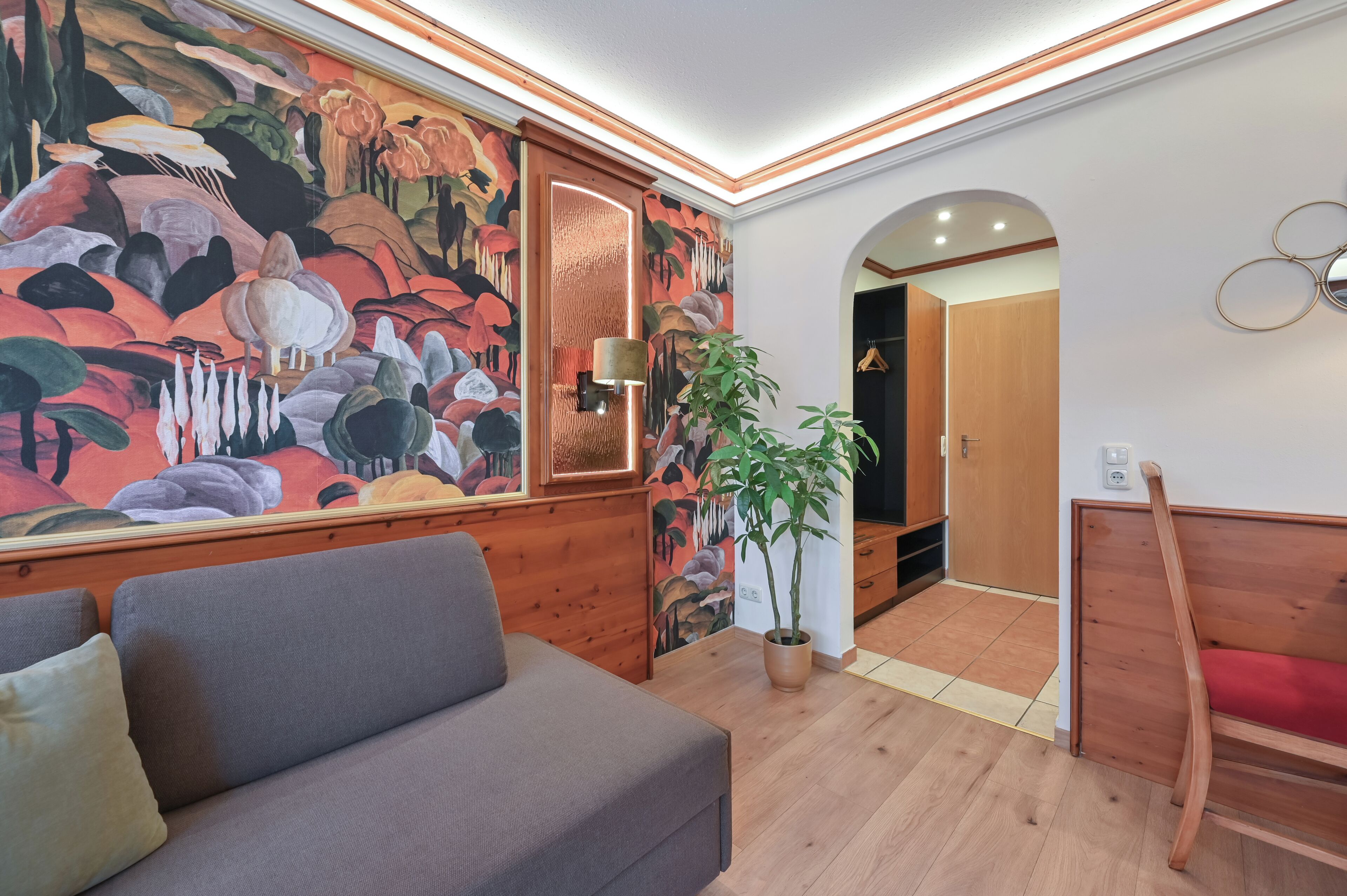 Uma sala de estar moderna com um sofá cinzento, um grande painel floral, um armário de madeira e uma planta em vaso.