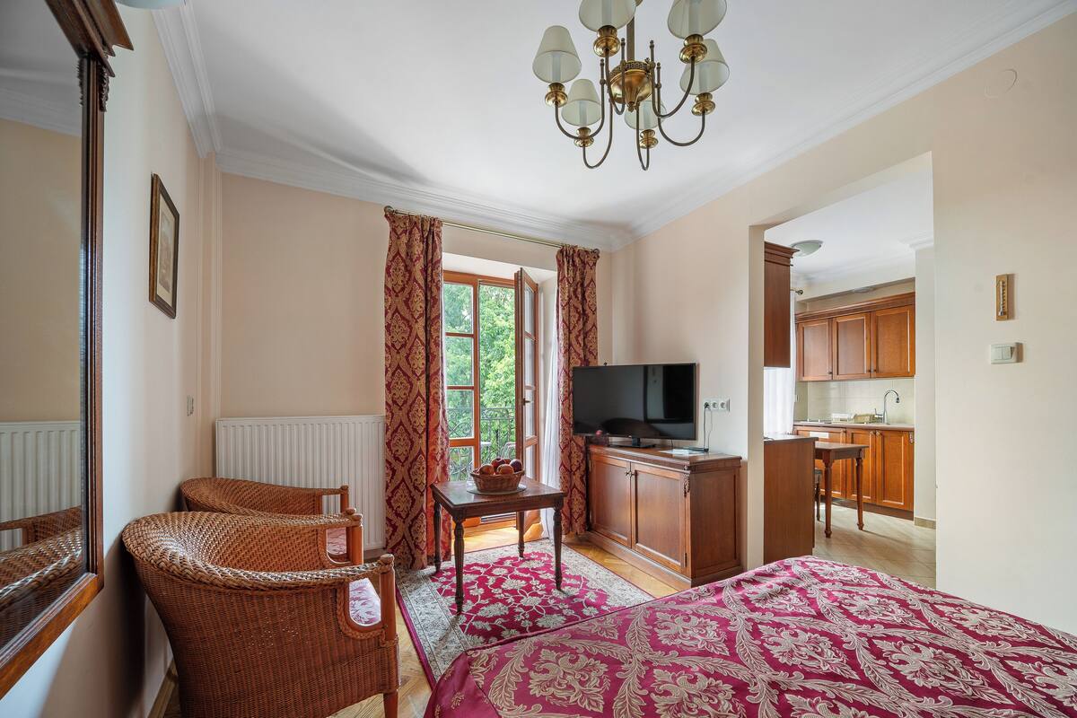 Quarto com cama, televisão, mobiliário de vime, mesa de jantar e vista para cozinha.