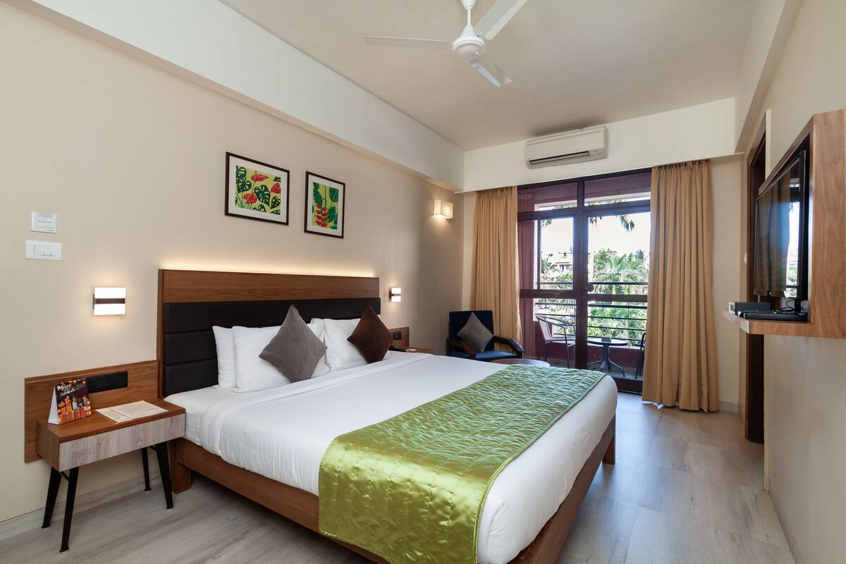 Quarto de hotel com cama, escrivaninha, cadeira, televisão e varanda com vista.