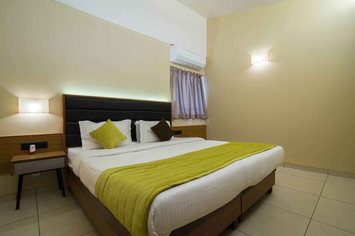 Quarto de hotel com uma cama, mesas de cabeceira, ar condicionado e janela com cortinas.