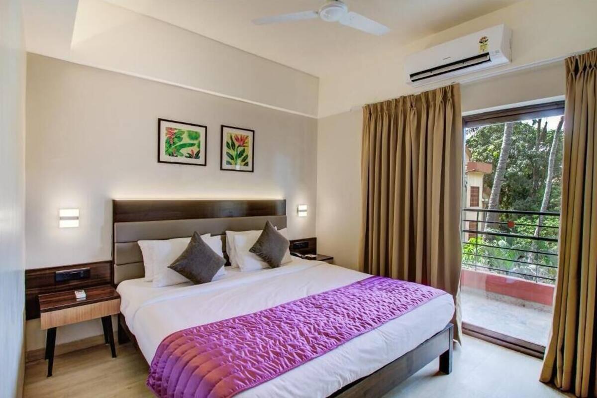 Quarto de hotel com cama, mesas de cabeceira, unidade de ar condicionado, ventilador de teto e varanda com cortinas.