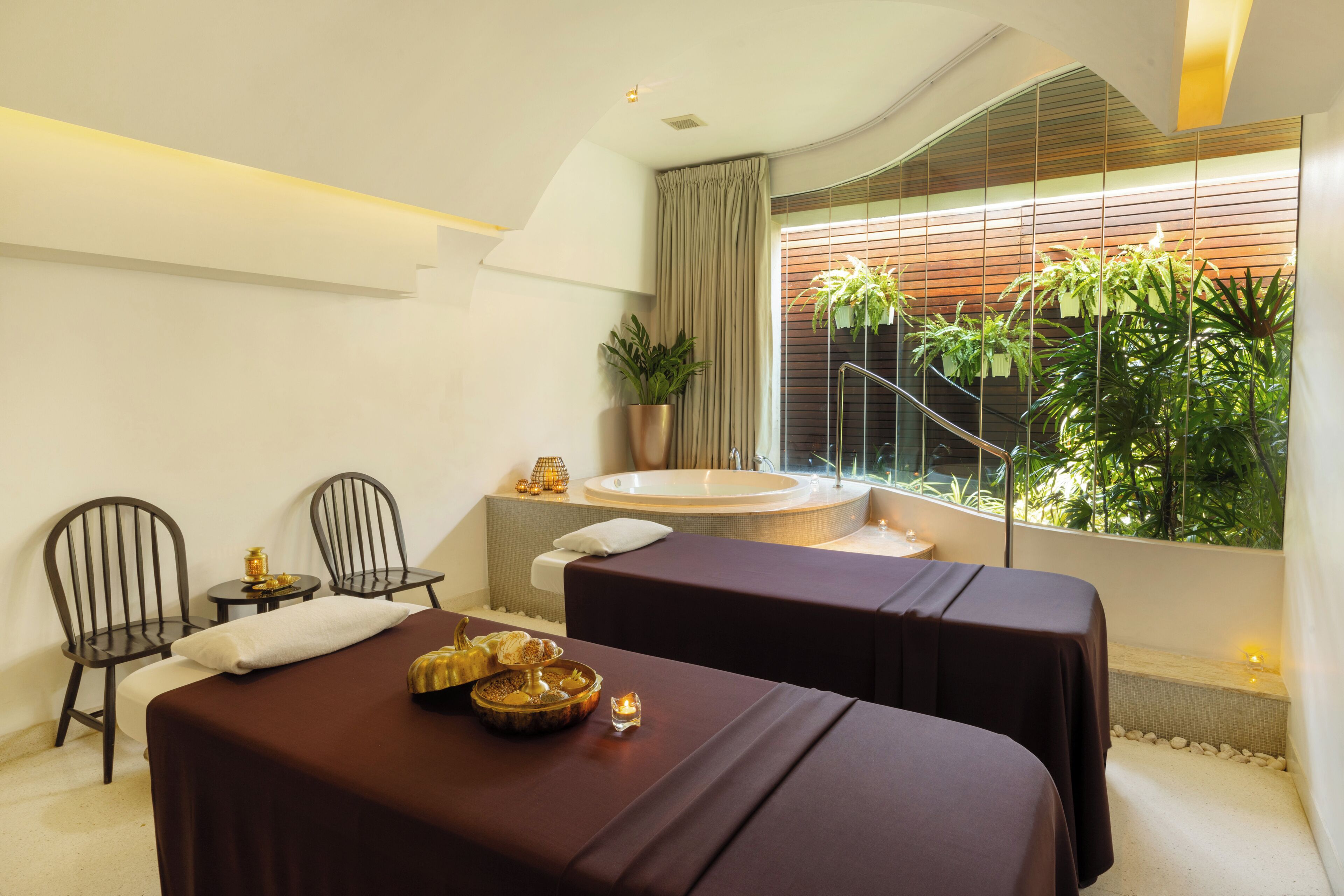 Uma sala de spa com duas macas de massagem, uma banheira e uma janela com plantas.