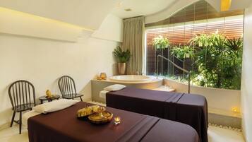 Uma sala de spa com duas macas de massagem, uma banheira e uma janela com plantas.