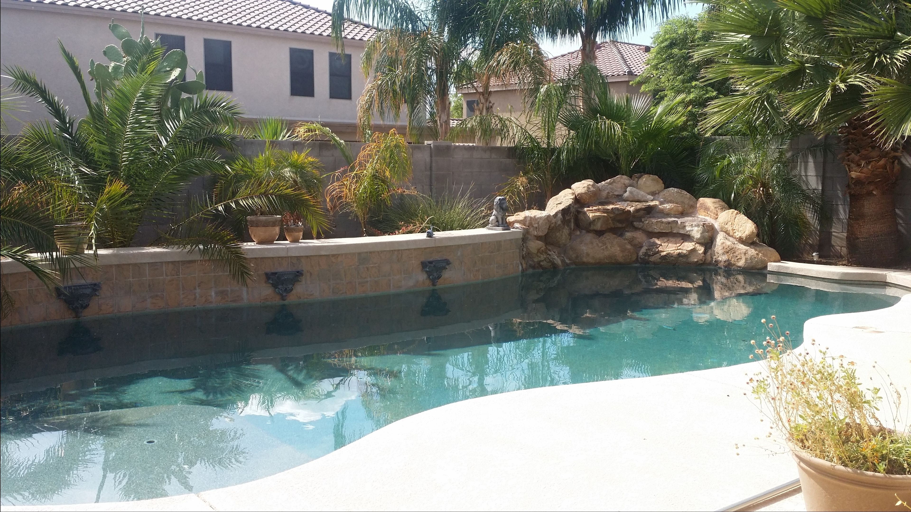 Piscina com muro de pedra, palmeiras e uma estátua.