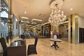 Um hall amplo com um lustre moderno, uma mesa de vidro e vista para o exterior.
