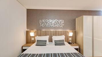 Quarto de hotel moderno com uma cama grande, duas mesas de cabeceira, um painel decorativo na parede e um guarda-roupa.