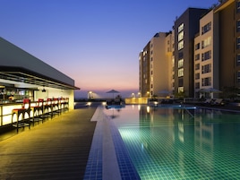 Uma área de piscina no terraço, com bar e espreguiçadeiras, rodeada por edifícios altos.