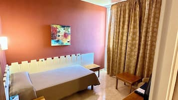 Quarto de hotel com cama, escrivaninha, cadeira, ventoinha no teto, quadro na parede e janela com cortinas.