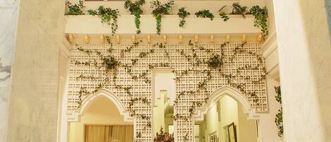 Um amplo saguão com teto alto, um piano, área de estar e uma parede decorativa com plantas trepadeiras.