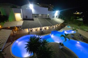 Piscina com design curvo, cercada por palmeiras e áreas de estar ao ar livre.