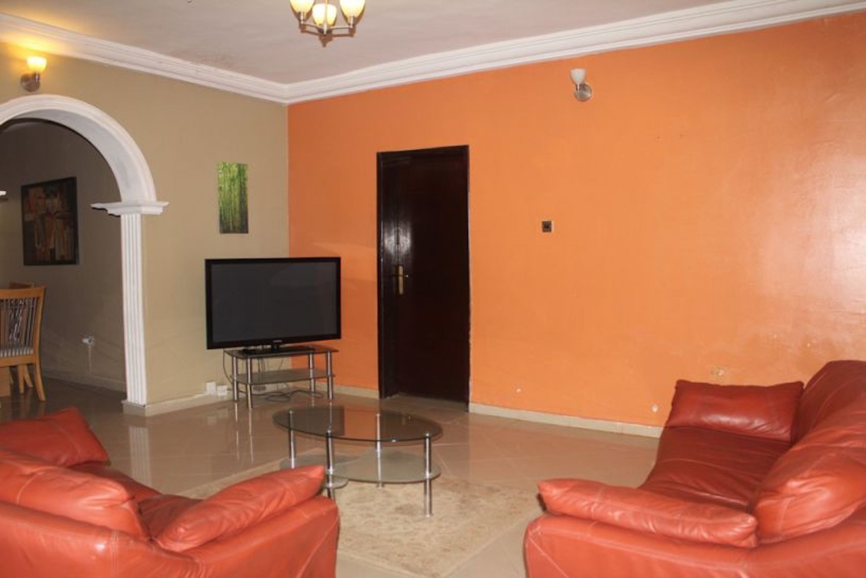 Sala de estar com paredes laranja, uma porta preta, uma televisão de tela plana em um suporte e dois sofás de couro vermelho.