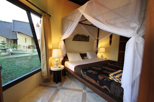 Quarto com cama, duas luminárias de cabeceira, janela com cortinas e vista para o exterior.