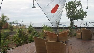 Uma área de estar ao ar livre com cadeiras de vime e um deck de madeira com vista para o mar.