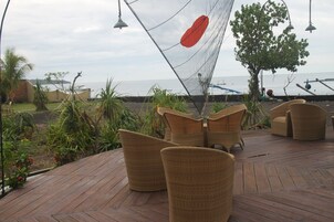 Uma área de estar ao ar livre com cadeiras de vime e um deck de madeira com vista para o mar.