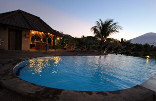 Uma piscina com deck ladrilhado, área de bar com teto em azulejos e uma montanha ao fundo.