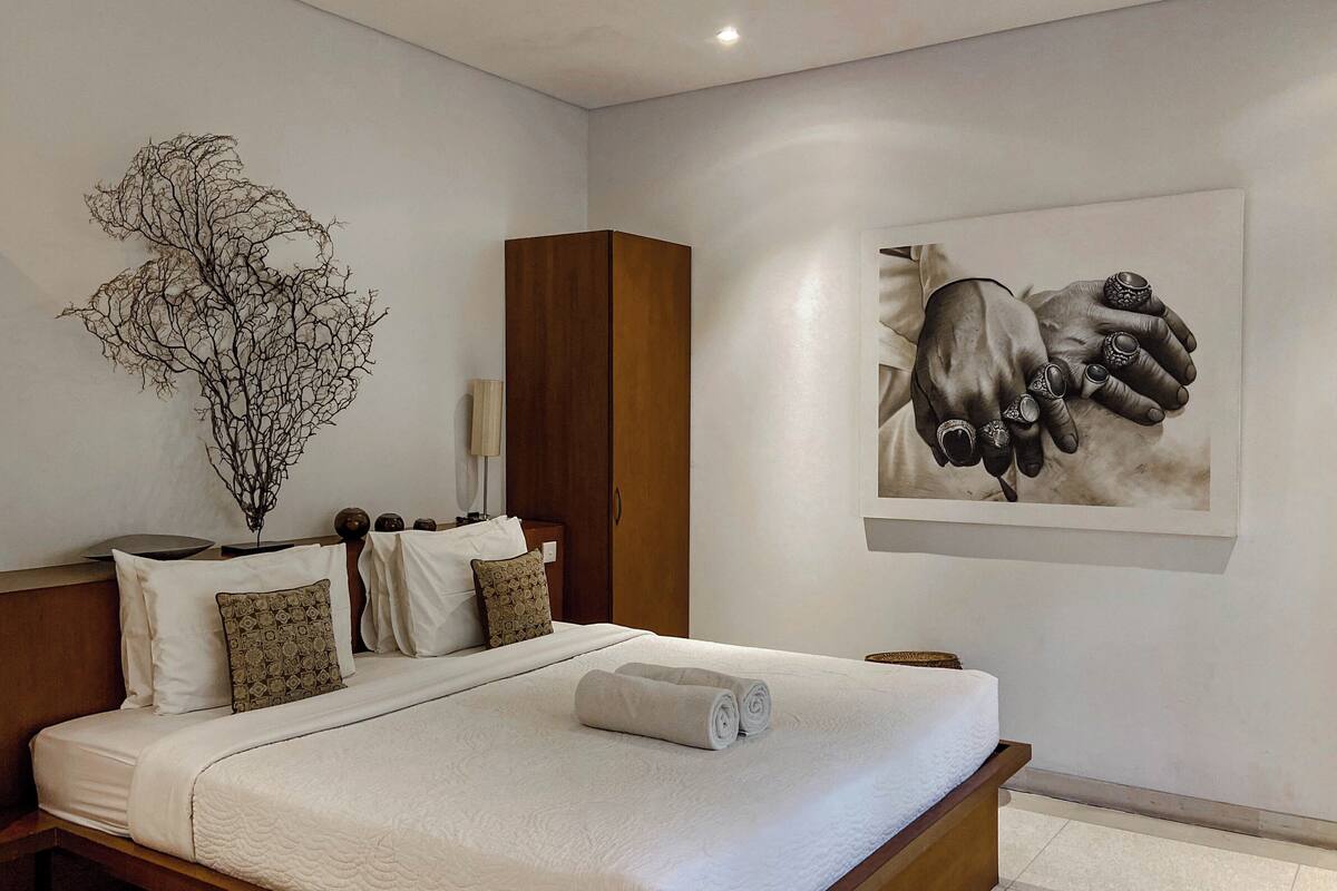 Quarto com cama grande, guarda-roupa, obra de arte na parede e planta decorativa.