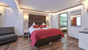 Quarto de hotel moderno com uma cama grande, um sofá, uma escrivaninha e um banheiro visível por uma porta aberta.