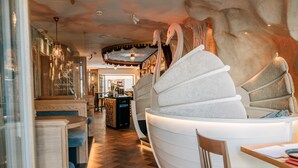 Restaurante com uma área de estar em formato de cisne, piso de madeira e um candelabro.