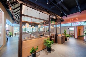 Uma área de recepção com balcão de madeira, plantas em vasos e luminárias pendentes.