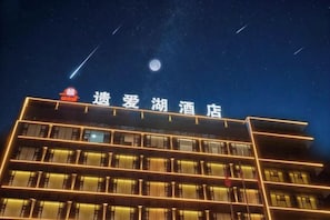 Hotel com placa em caracteres chineses, vários andares e céu estrelado.