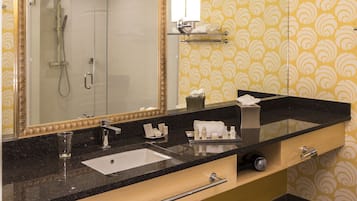 Um banheiro de hotel com um espelho grande, pia, porta-toalhas e área de chuveiro.