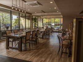 Um restaurante com mesas e cadeiras de madeira, janelas amplas e vista para o exterior.