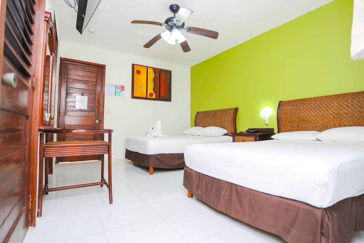 Quarto de hotel com cama, escrivaninha, cadeira, ventilador de teto e uma parede com um quadro.